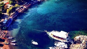 Vista aérea de uma área costeira com barcos atracados na orla e um barco grande ancorado próximo ao centro.