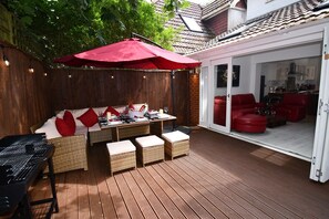 Um pátio externo com uma mesa de jantar, almofadas vermelhas e um guarda-sol vermelho.