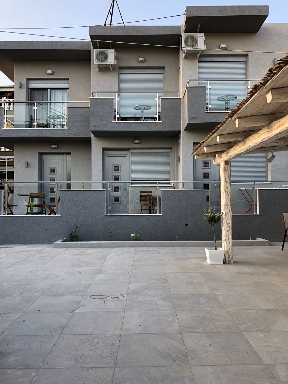 Um edifício moderno com telhado plano, grandes janelas e área externa coberta com pérgola de madeira.