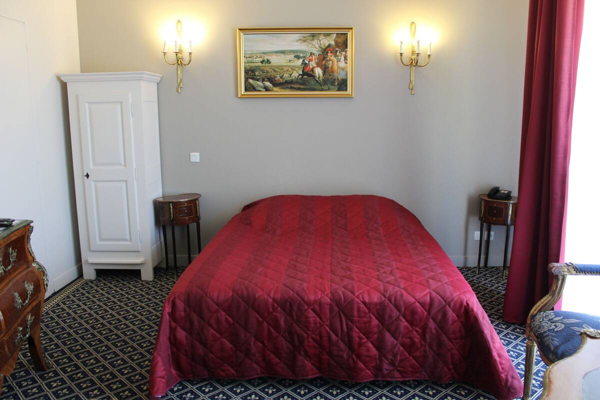 Quarto com uma cama grande, um guarda-roupa branco, uma mesinha e um quadro na parede.