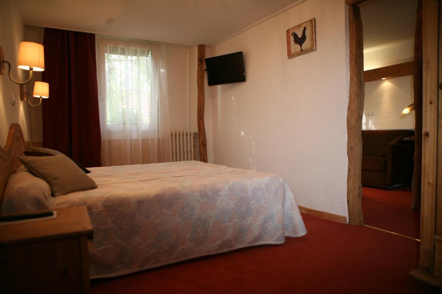 Quarto com cama, televisão fixada na parede e porta de madeira que dá para outro cômodo.