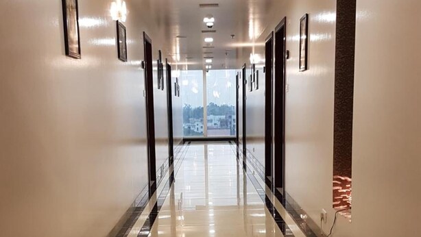 Um corredor longo e bem iluminado, com piso brilhante, quadros nas paredes e vista para edifícios lá fora.