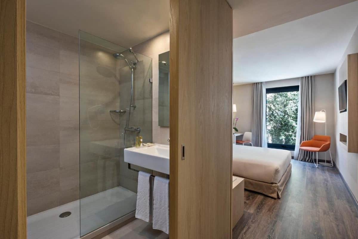 Uma casa de banho de hotel moderna com chuveiro em cabine de vidro, lavatório e espelho.