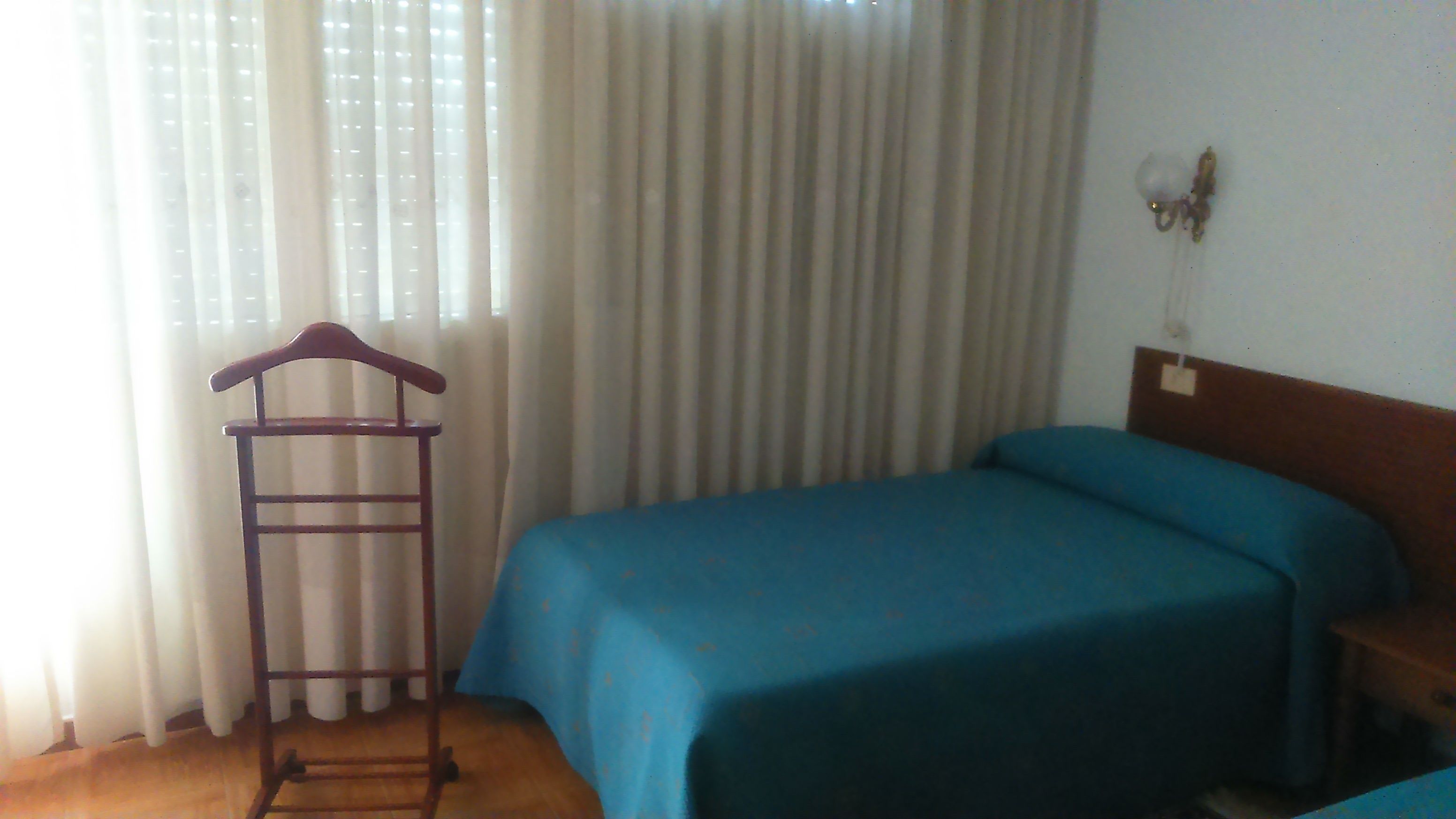 Quarto com cama, cabideiro de madeira e janela com cortinas.