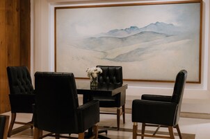Quarto com uma grande pintura de paisagem montanhosa na parede, um sofá de couro preto e uma pequena mesa com um vaso de flores.
