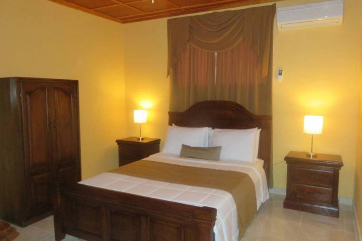 Um quarto com cama de madeira, duas mesas de cabeceira com luminárias, um guarda-roupa e uma cortina.