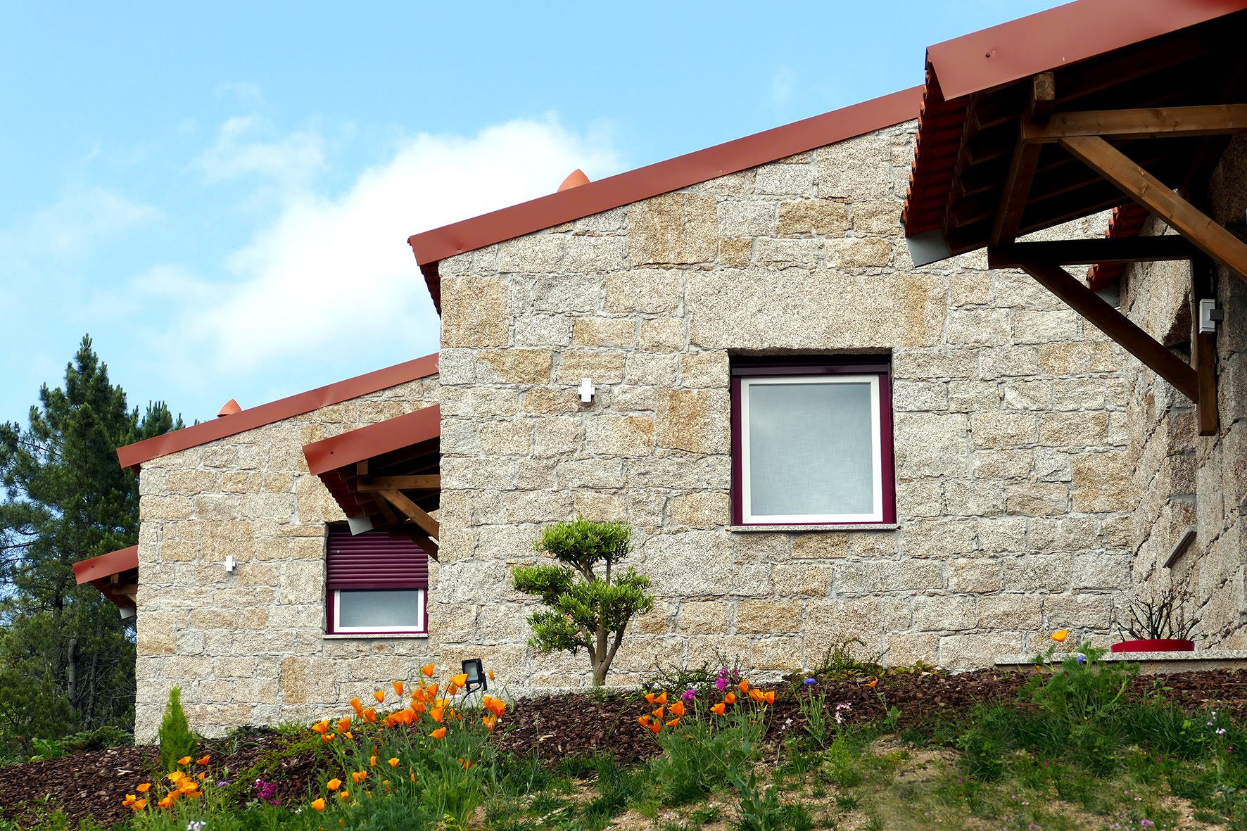 Um edifício de pedra com telhado vermelho, uma pequena janela e um jardim com flores.