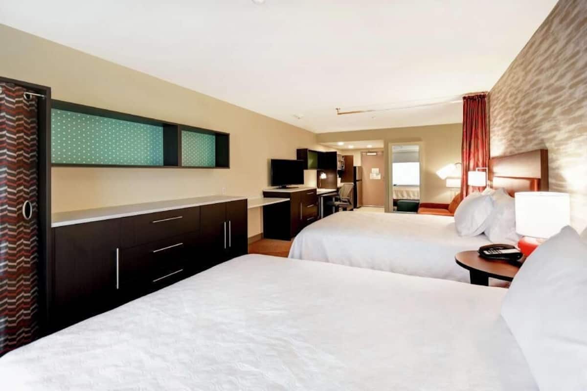 Quarto de hotel com duas camas, televisão, escrivaninha e banheiro visível através de uma porta aberta.