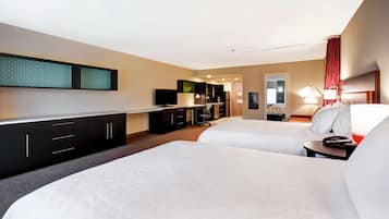 Quarto de hotel com duas camas, uma escrivaninha, televisão e cozinha compacta.