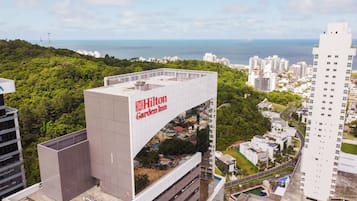 Edifício do Hilton Garden Inn com design moderno, rodeado por vegetação exuberante e vista para o mar.