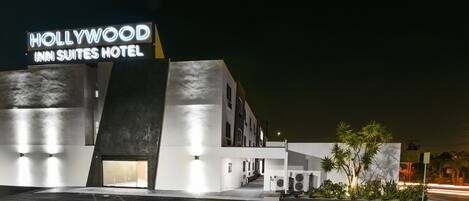 Exterior do Hotel Hollywood Inn Suites, com um letreiro de neon chamativo, design arquitetônico moderno e estacionamento.
