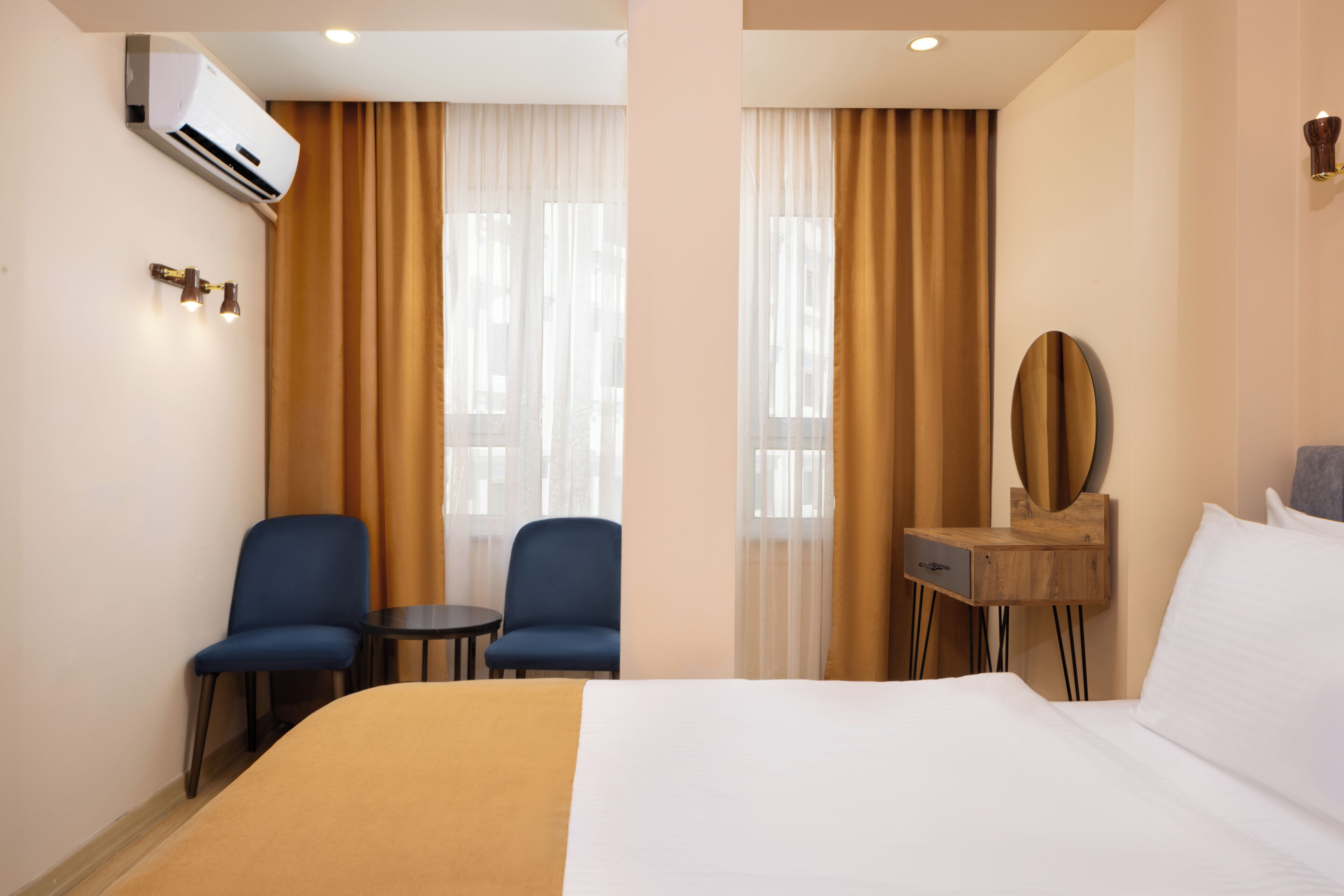 Quarto de hotel com cama, duas cadeiras, uma mesa pequena, ar condicionado e espelho.