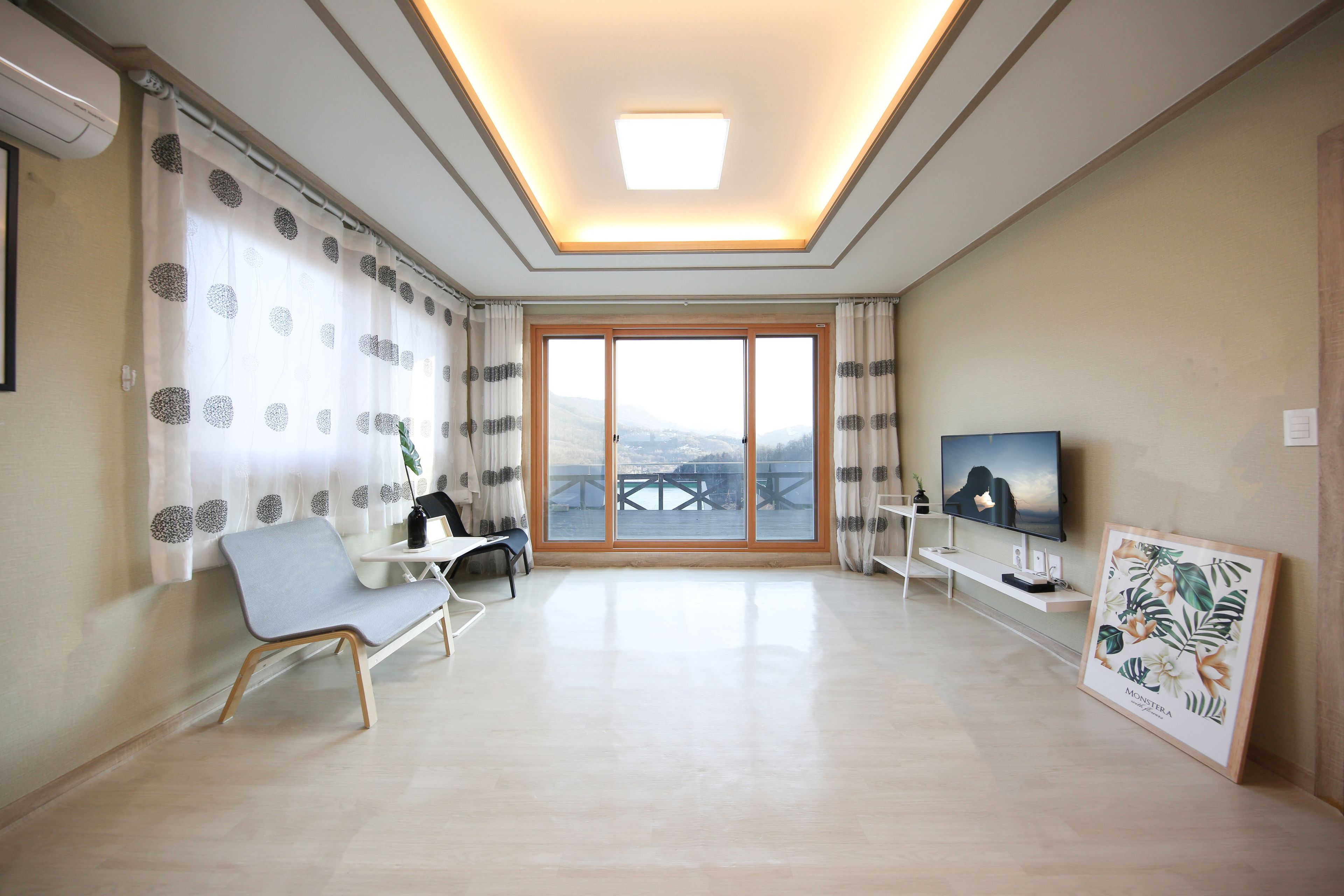 Uma sala de estar moderna com uma janela grande, uma televisão de tela plana, uma impressão botânica emoldurada e uma área de estar com um banco e uma mesa.
