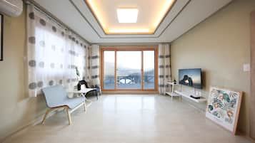 Uma sala de estar moderna com uma janela grande, uma televisão de tela plana, uma impressão botânica emoldurada e uma área de estar com um banco e uma mesa.