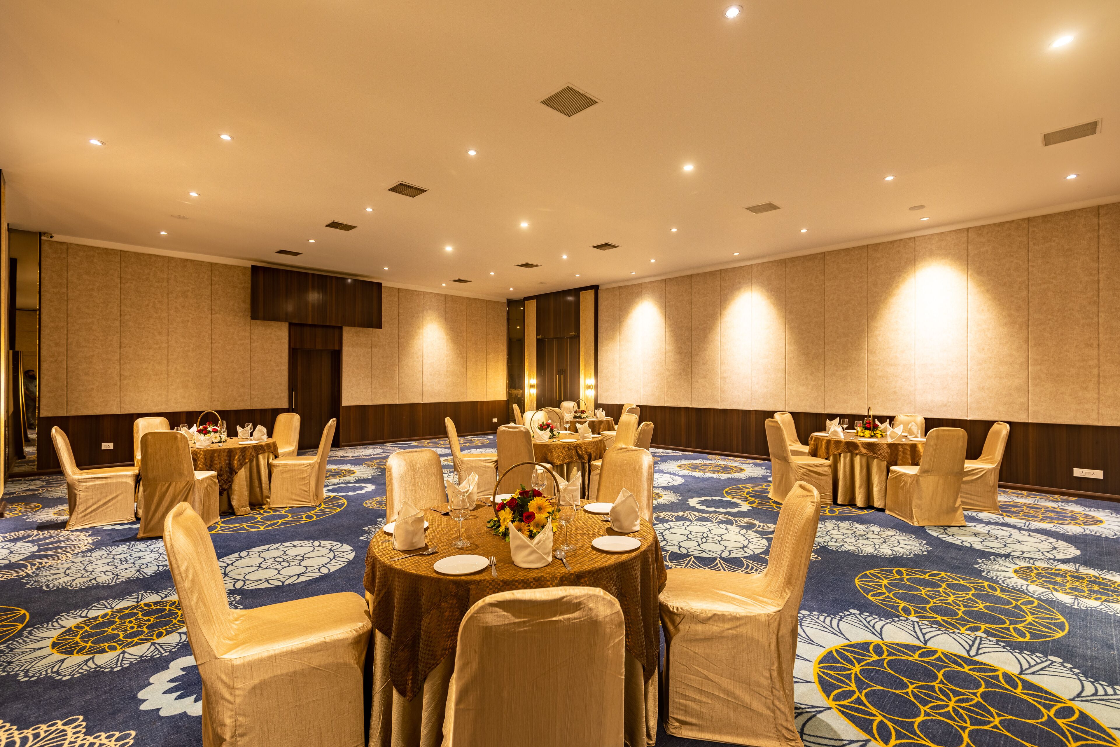 Uma sala de banquetes com mesas redondas, cadeiras e piso coberto de carpete.