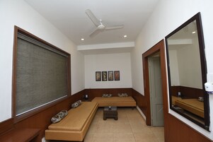 Um quarto com uma janela grande, um ventilador de teto, um sofá, uma mesinha e um espelho.