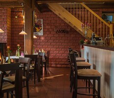 Um restaurante com paredes de tijolo, cadeiras e mesas de madeira e uma escadaria.