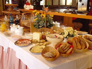 Uma mesa de buffet com diversos alimentos, incluindo pão, queijo e doces, dispostos sobre uma toalha branca.