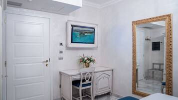 Quarto de hotel com porta branca, escrivaninha com cadeira, quadro na parede e um espelho grande com moldura dourada.