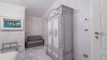 Quarto com um guarda-roupa grande e branco, um sofá cinzento e uma televisão na parede exibindo uma vista panorâmica.