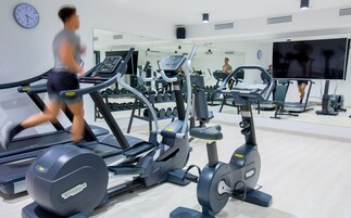 Academia com esteiras, halteres e uma tela de televisão.