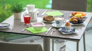 Uma mesa de café da manhã com diversos alimentos, uma xícara de café e um pequeno vaso de planta.