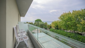 Varanda com guarda-corpo de vidro, vista para um jardim ajardinado e um corpo d'água.