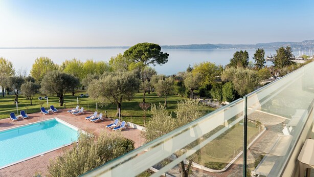 Piscina com espreguiçadeiras, vista deslumbrante para o mar e área gramada com árvores.