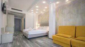 Quarto de hotel moderno com cama, um sofá amarelo e uma pequena mesa.