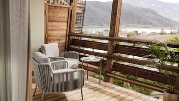 Um deck de madeira com uma cadeira e uma mesa pequena, com vista para um lago e montanhas.