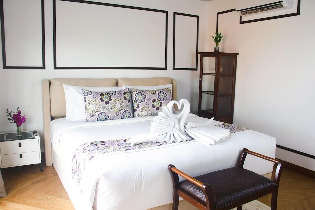 Cama bem arrumada com almofadas estampadas de flores e toalha dobrada em formato de cisne.