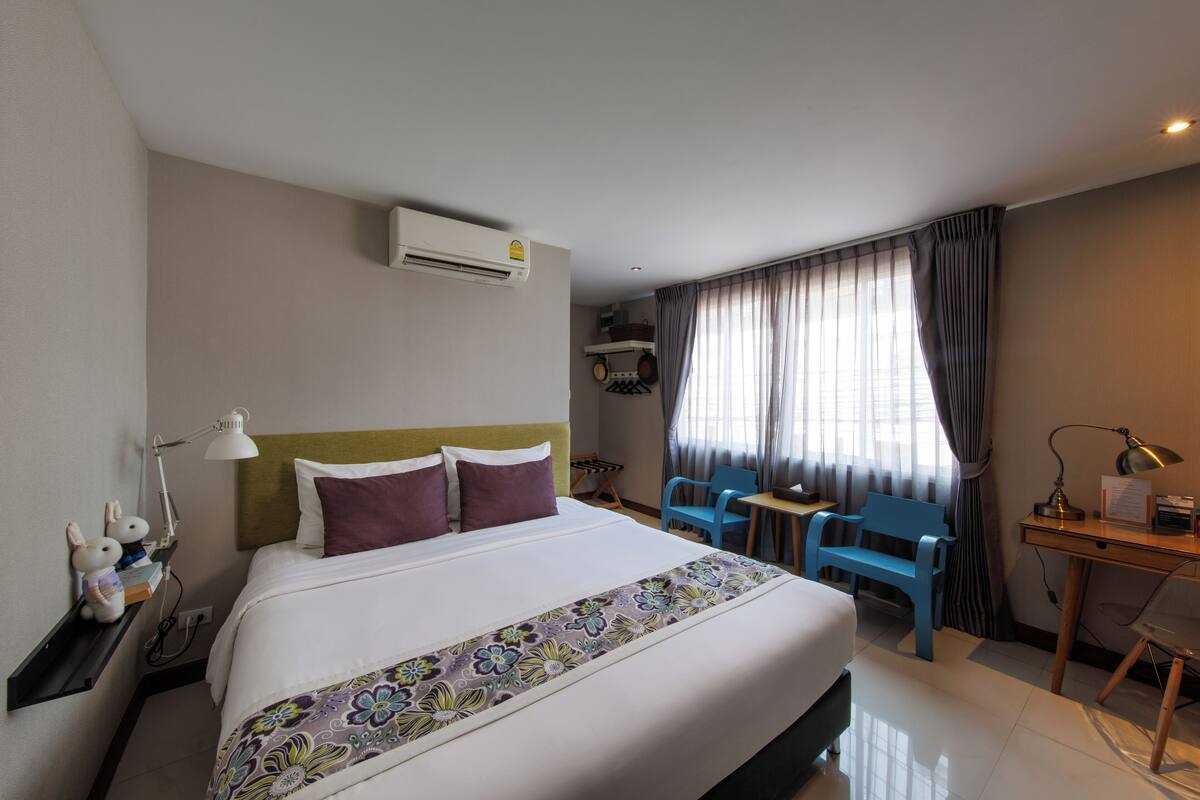 Quarto de hotel com uma cama grande, uma escrivaninha, uma cadeira e uma janela com cortinas.