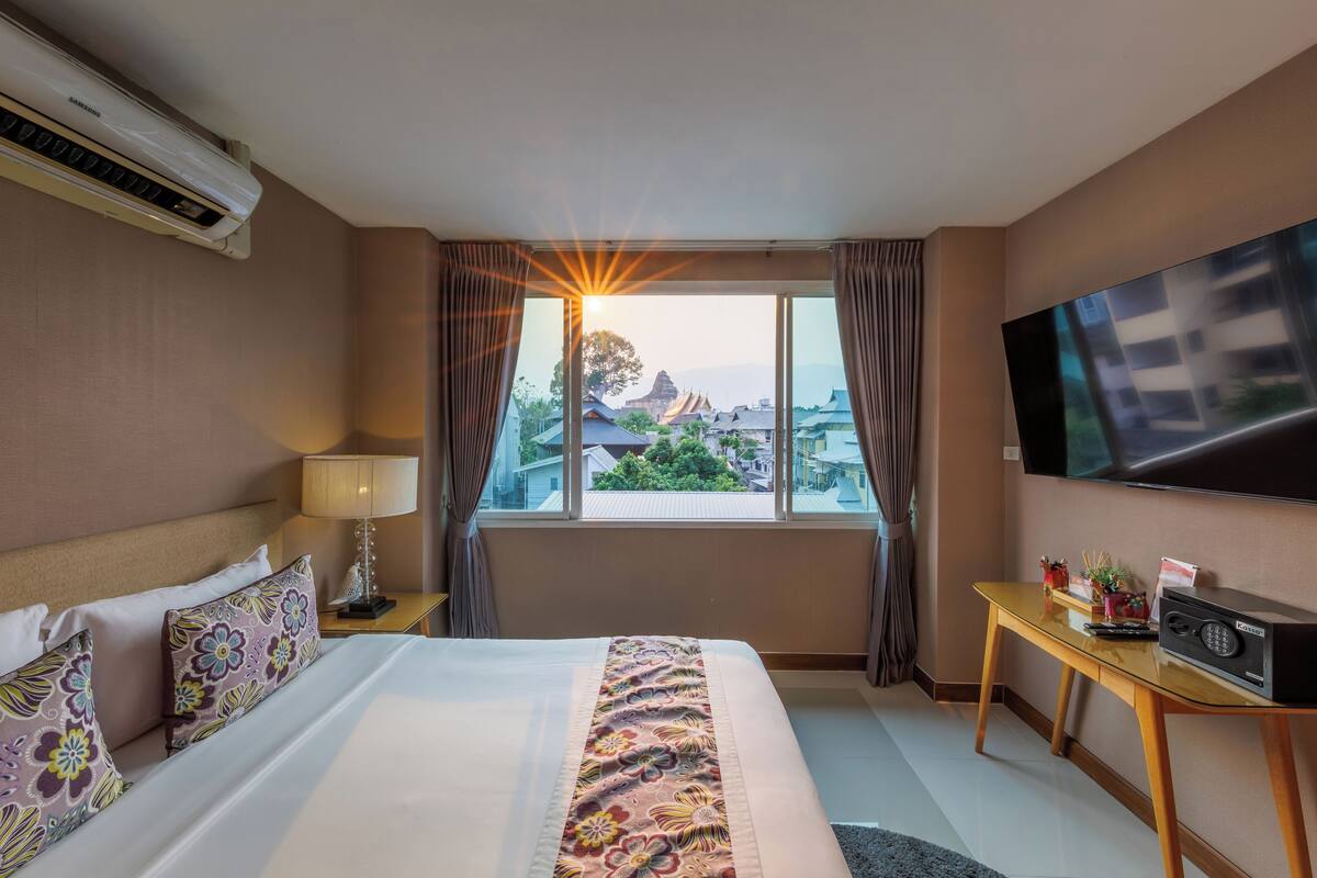 Quarto de hotel com cama, televisão, escrivaninha e janela com vista para um templo e edifícios.