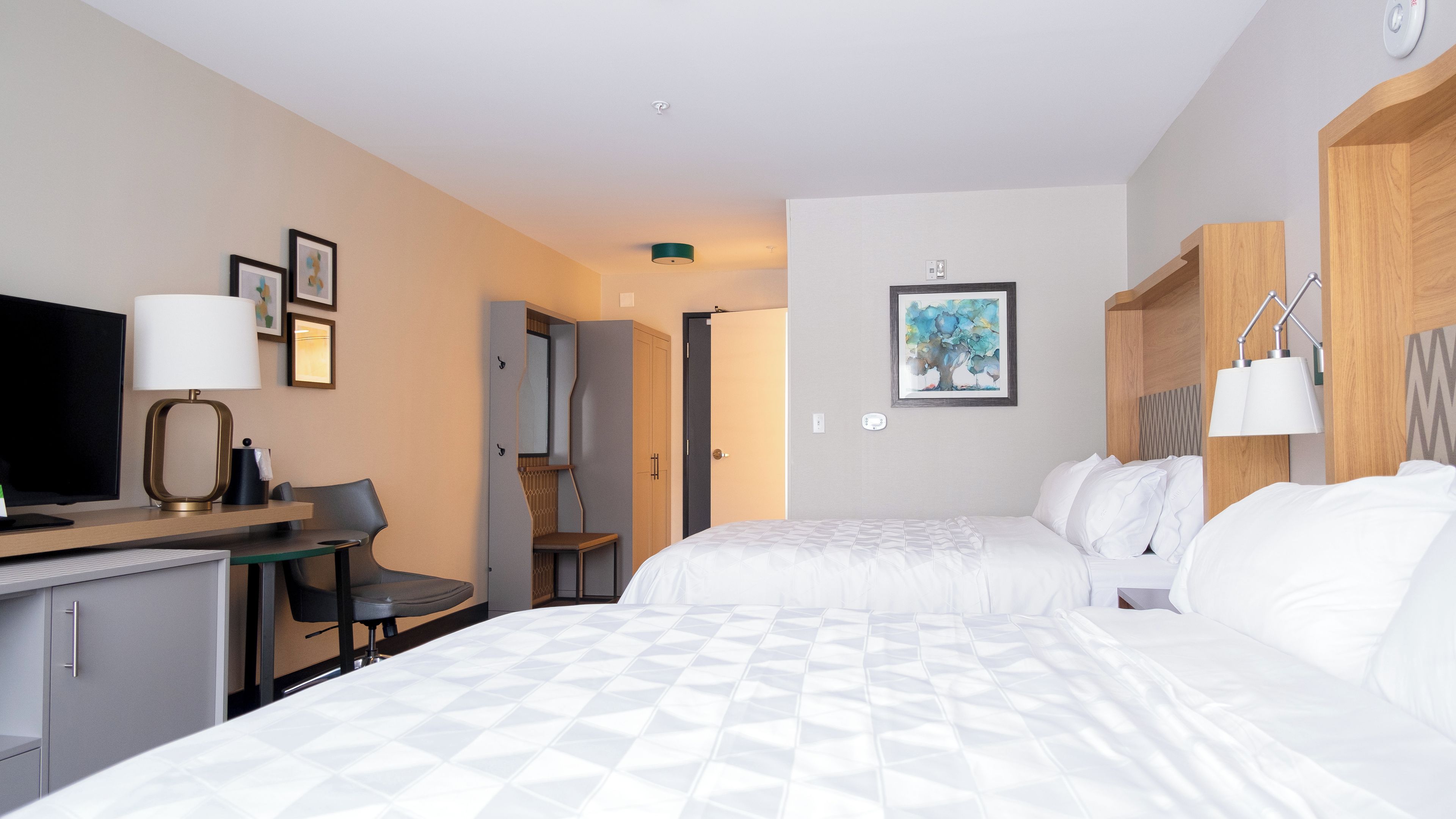 Quarto de hotel com cama, escrivaninha, cadeira, televisão e um quadro na parede.