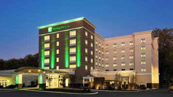 Um hotel Holiday Inn & Suites com design moderno, destacando uma placa verde chamativa, vários andares e uma entrada bem iluminada.