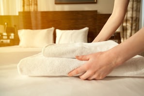 Cama bem arrumada com roupa de cama e almofadas brancas, cabeceira de madeira e mesa de cabeceira com abajur.