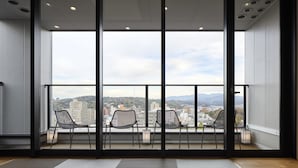Quarto com uma janela grande, duas cadeiras e vista para a paisagem urbana.