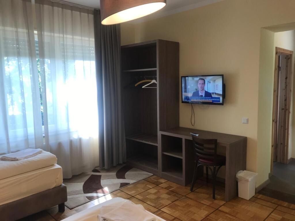 Quarto de hotel com cama, escrivaninha, cadeira, televisão e guarda-roupa.