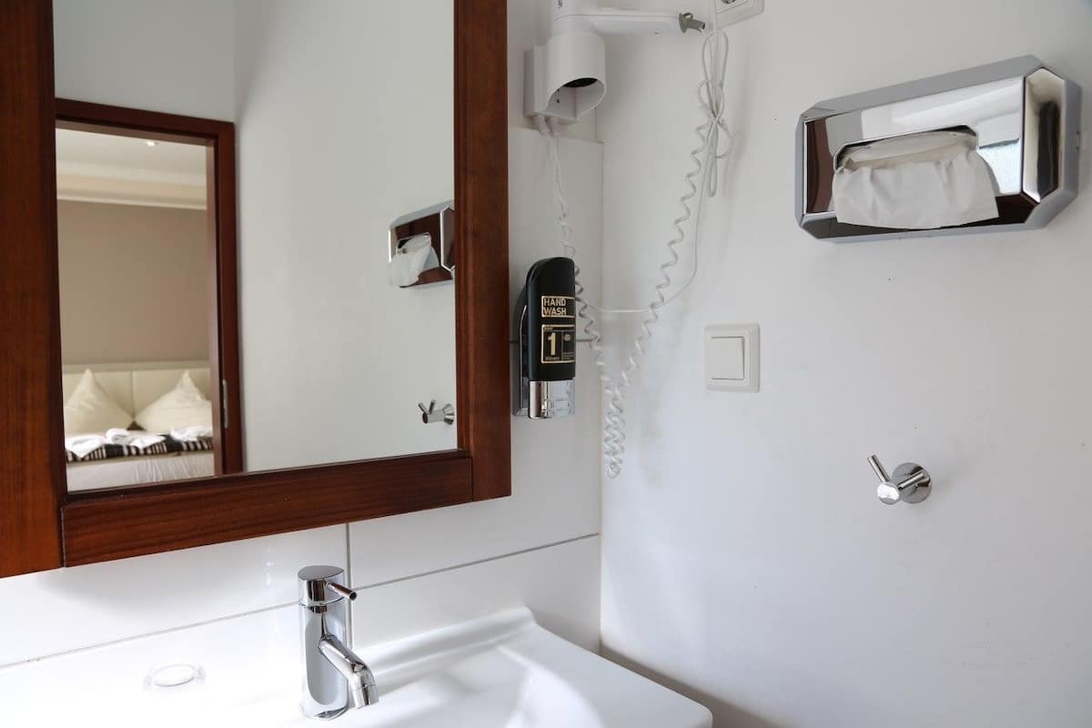 Casa de banho com lavatório branco, espelho com moldura de madeira, secador de cabelo e secador de mãos.