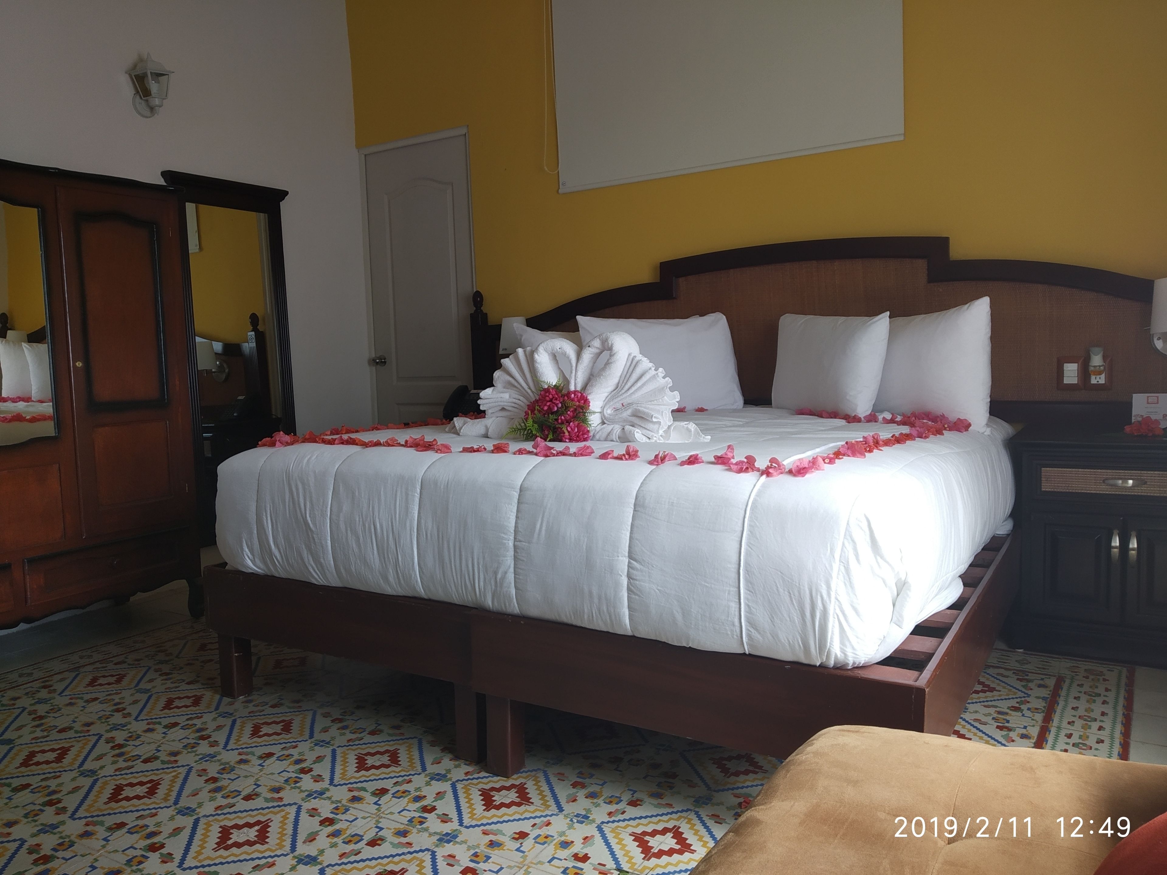 Quarto de hotel com uma cama grande, um guarda-roupa de madeira, um espelho e um chão com padrão.