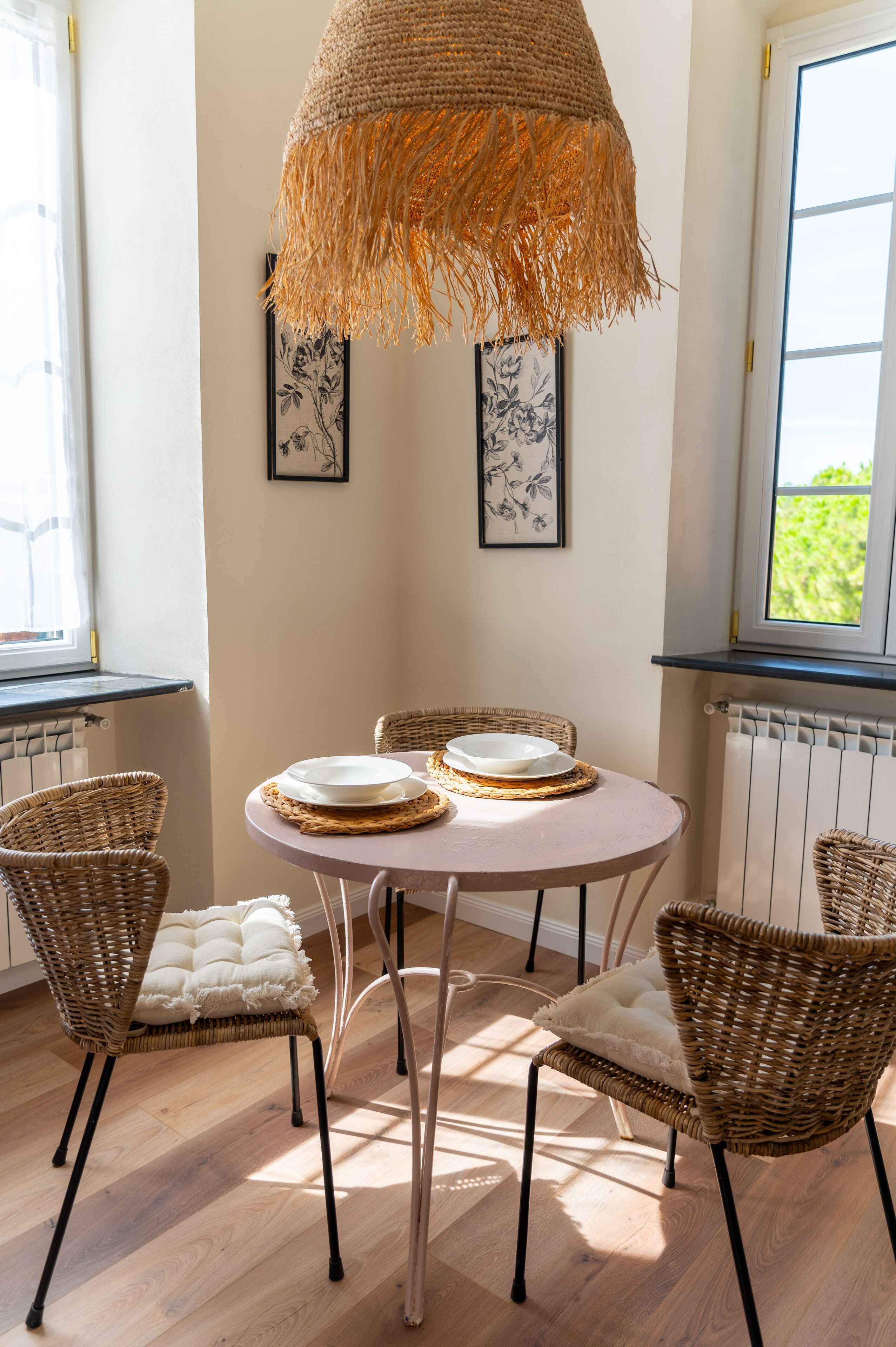 Uma sala de jantar com uma mesa redonda, cadeiras de vime e uma luminária pendente trançada.