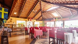 Restaurante com tetos de madeira alta, toalhas de mesa xadrez vermelhas e brancas e chão de azulejos.
