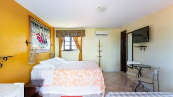 Quarto de hotel com cama, secretária, cadeira, ar condicionado e televisão na parede.