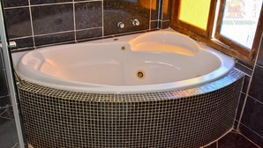 Uma banheira grande e independente com revestimento de mosaico, situada em um quarto com paredes revestidas de azulejos escuros e uma janela com vista.
