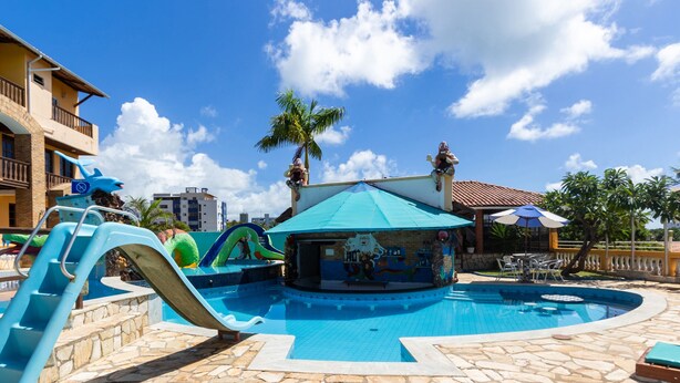 Piscina com escorregador, área de recreação infantil e bar com guarda-sóis.