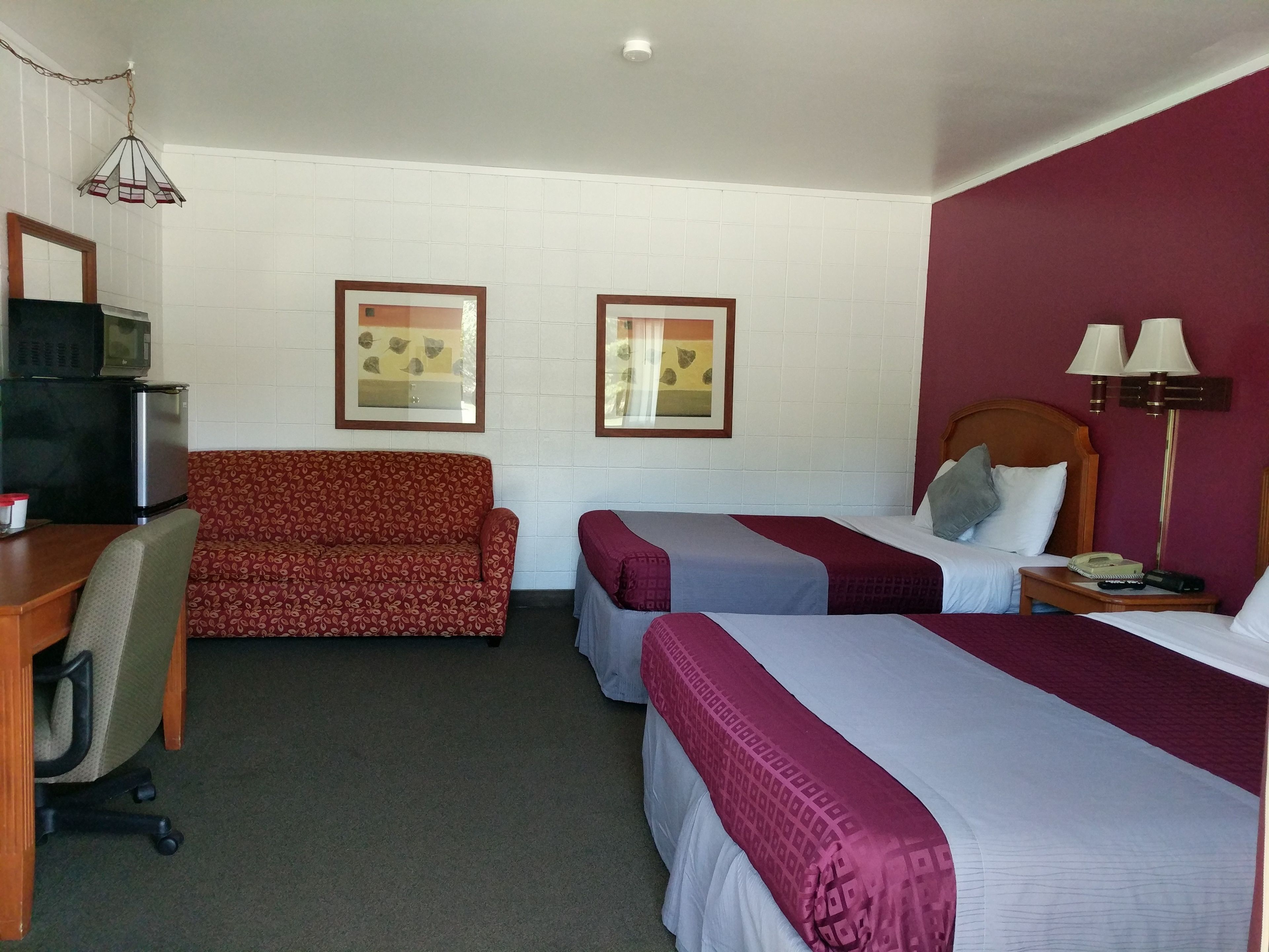 Quarto de hotel com duas camas, um sofá, uma escrivaninha com um computador e uma televisão.