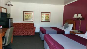 Quarto de hotel com duas camas, um sofá, uma escrivaninha com um computador e uma televisão.