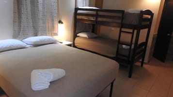 Quarto de hotel com uma cama de solteiro, uma cama beliche e uma mesa de cabeceira com abajur.