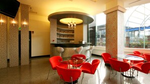 Um restaurante com cadeiras vermelhas e uma mesa de vidro, um candelabro e vista através de amplas janelas.