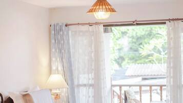 Quarto com cama de madeira, mesa de cabeceira, abajur e vista para o exterior através de uma janela com cortinas.